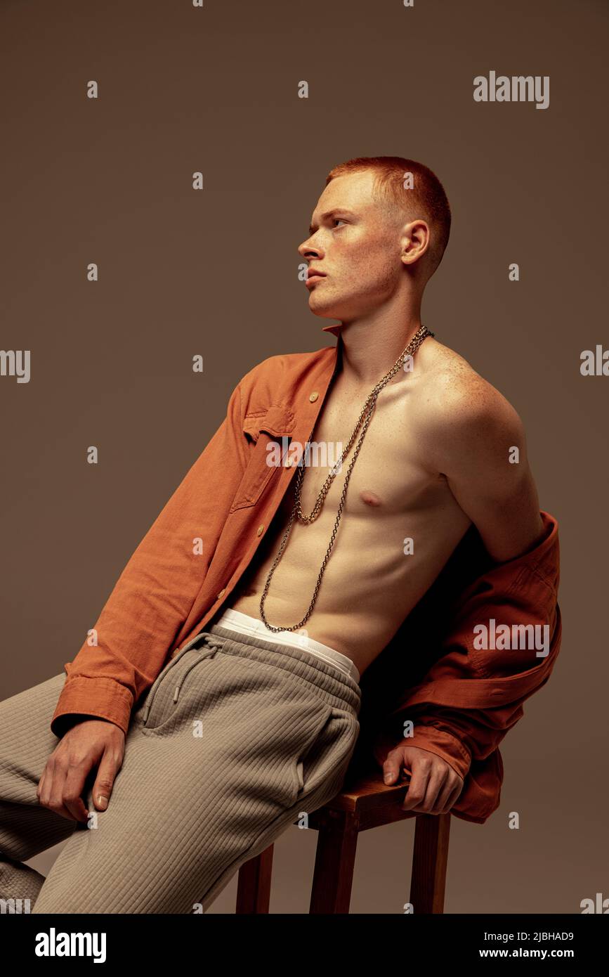Portrait of young stylish red-haired man sitting on chair, posing in ...