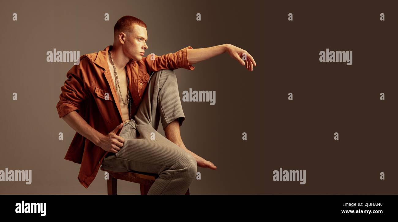Portrait of brutal young red-haired man, sitting on chair, posing ...
