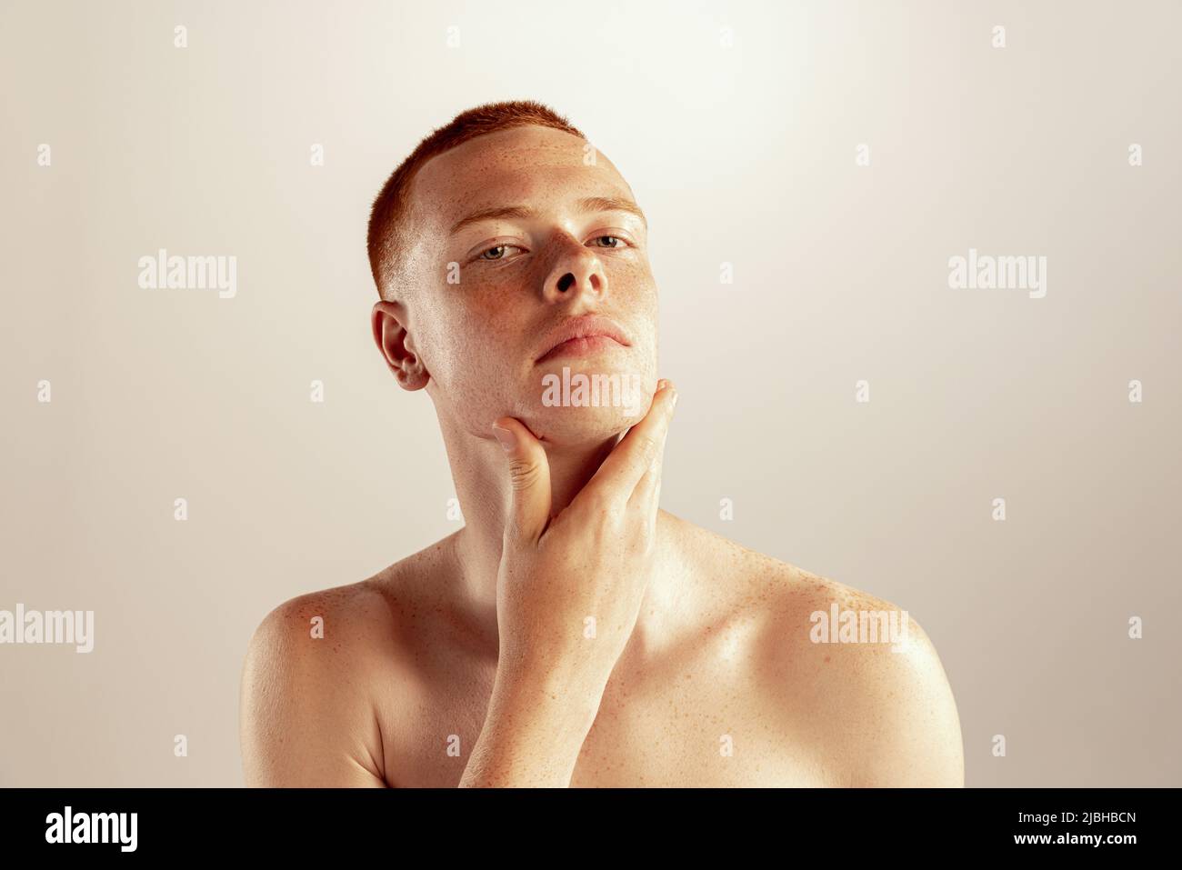 Portrait of young red-haired man with freckles touching cheeks, posing ...