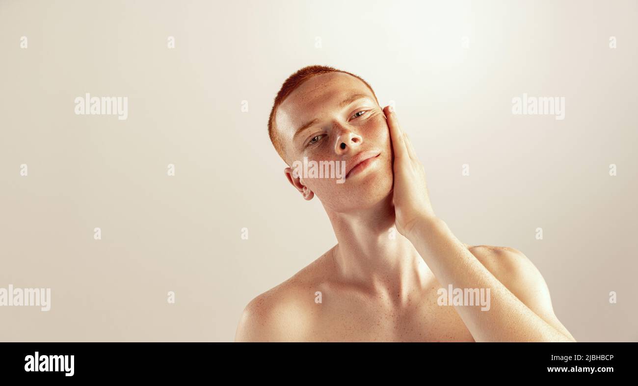 Portrait of young red-haired man with freckles touching cheeks, posing ...