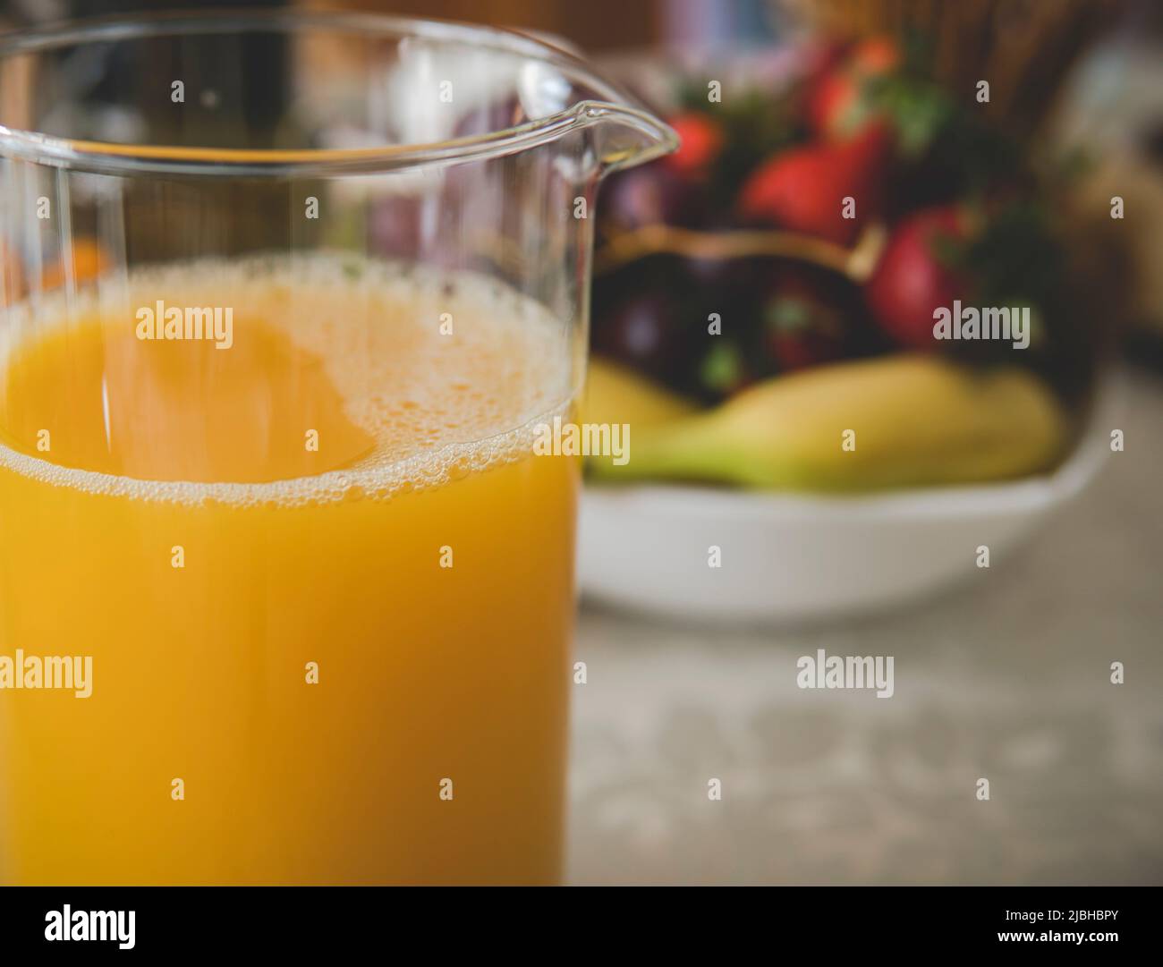 glass jar with an orange juice in front of a bowl full of fruits Stock ...