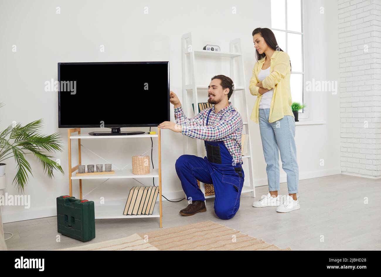 Young friendly service man installs and connects new TV in female ...