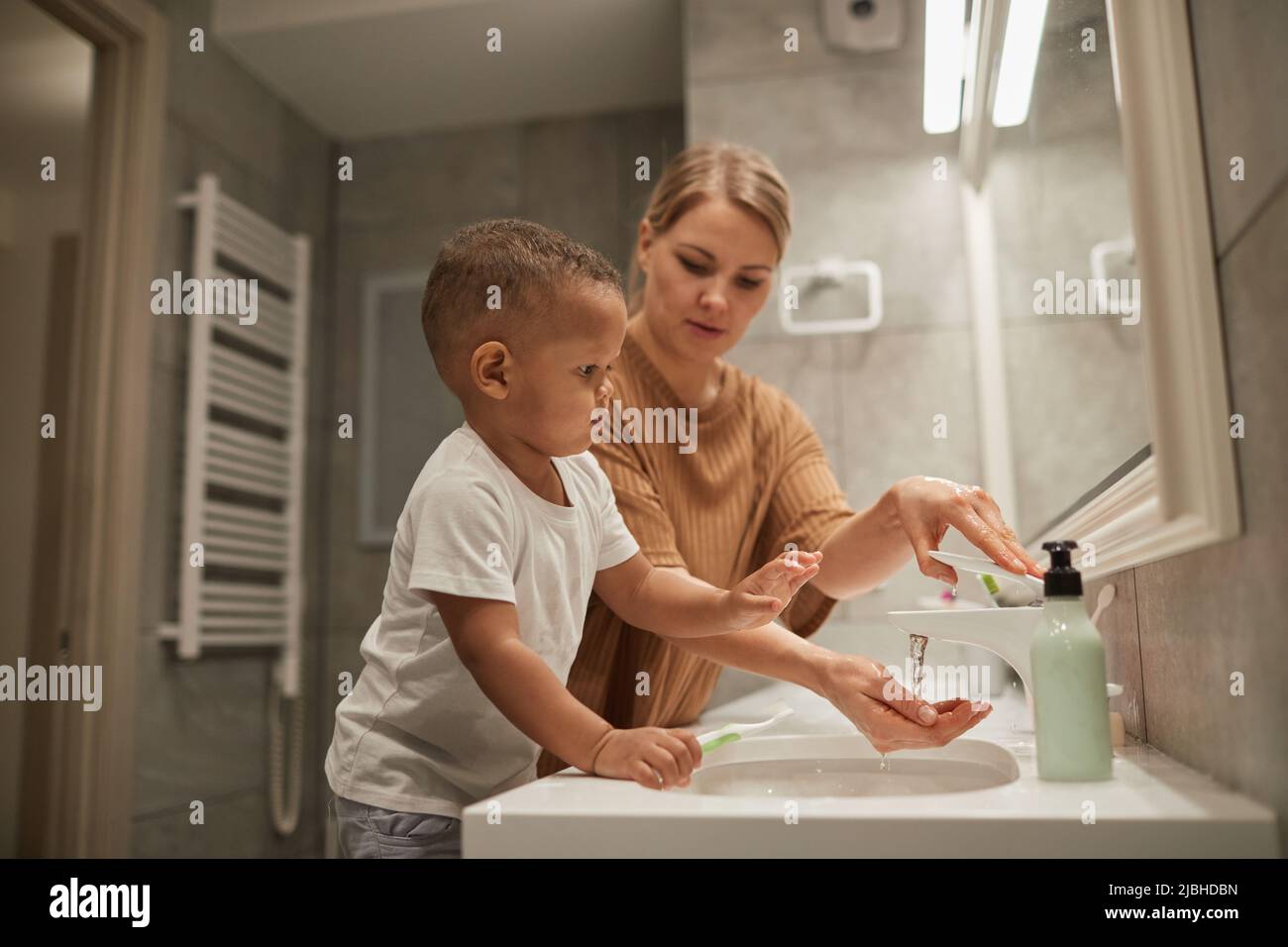 Portrait of young mother helping cute toddler boy brushing teeth in ...