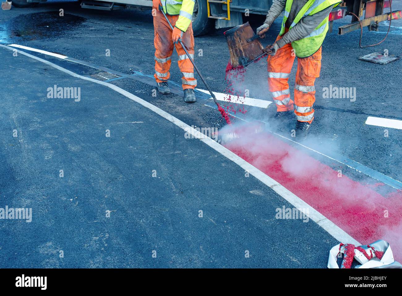 Road workers applying hot red road marking paint on new build road ...