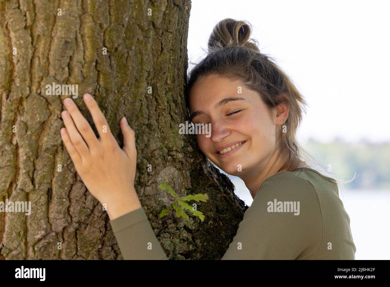 Contented young woman hugging a large tree with a blissful expression ...