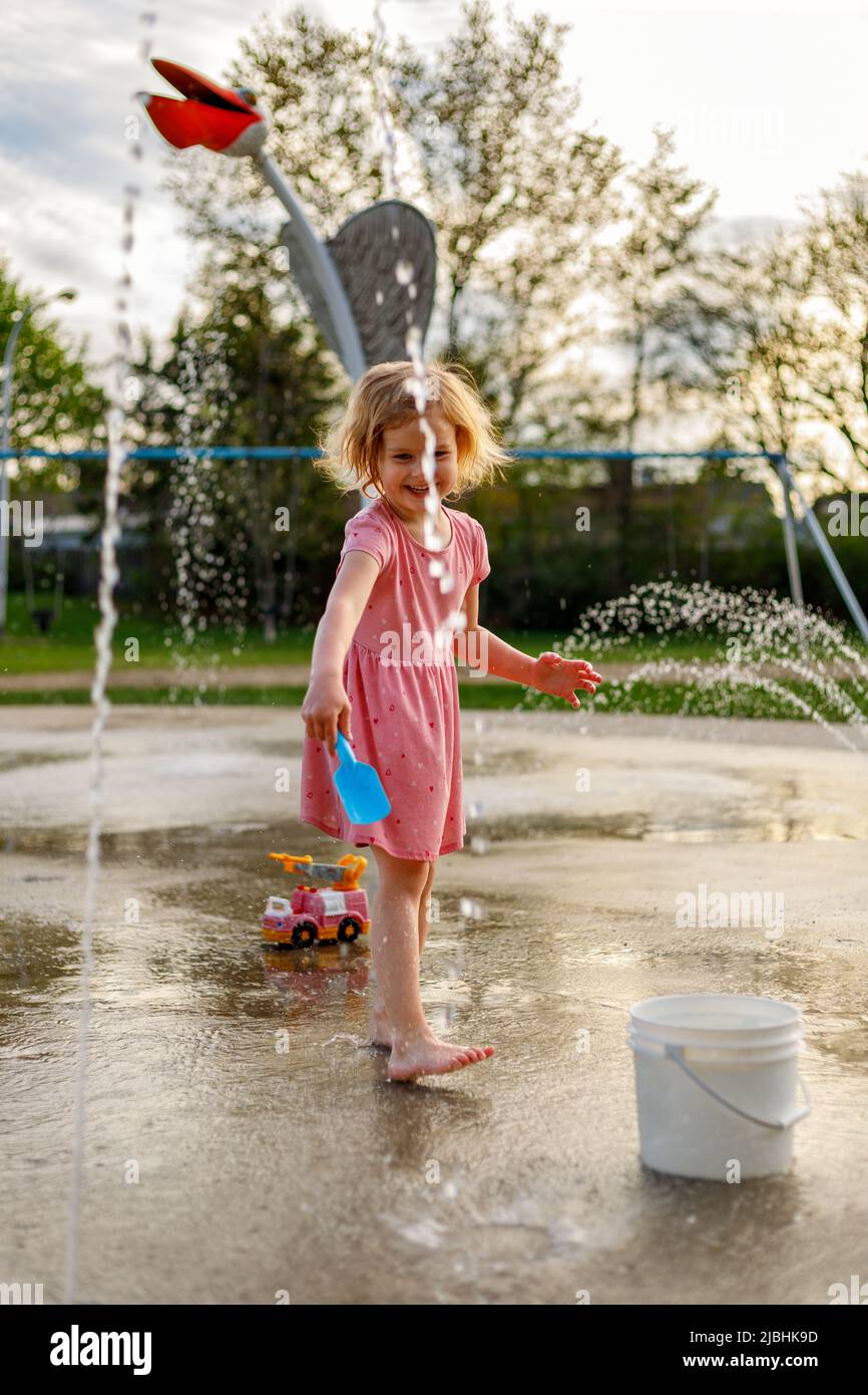 Happy smiling child playing with toys and water in park splash pad ...