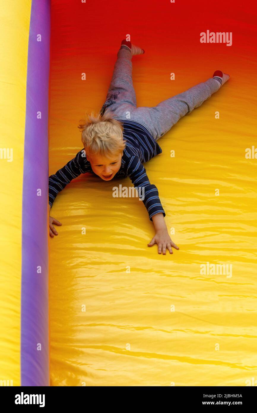 A brave little boy slides down on a red-yellow trampoline at an ...
