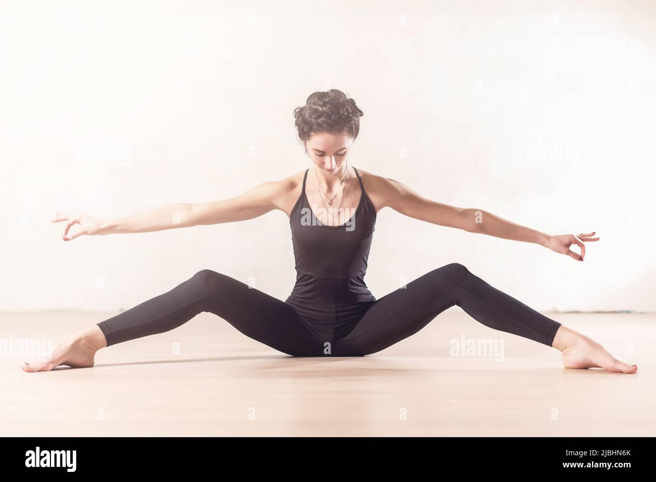 Slim young ballet dancer doing stretching exercise sitting with her ...