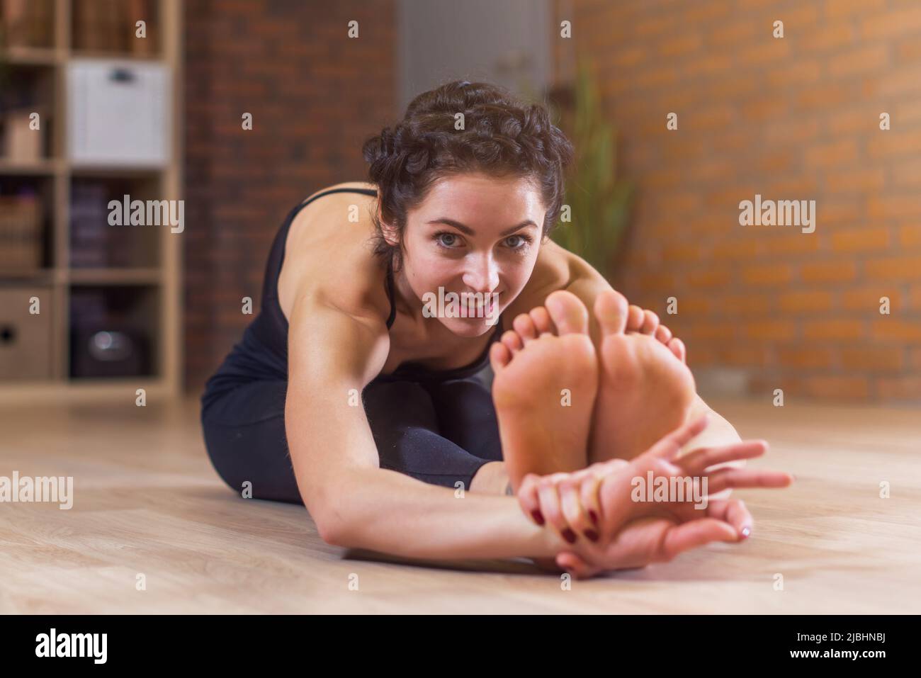 Pretty European woman sitting barefoot stretching her back and legs ...