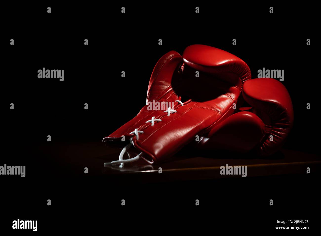 Shiny new red boxing gloves with laces in dim lighting on black ...
