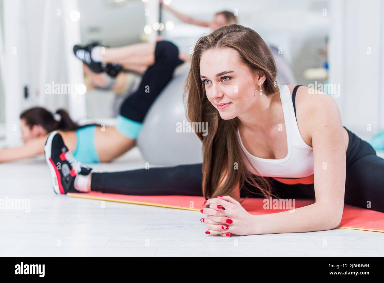 Cute smiling young lady in sportswear doing advanced middle split ...