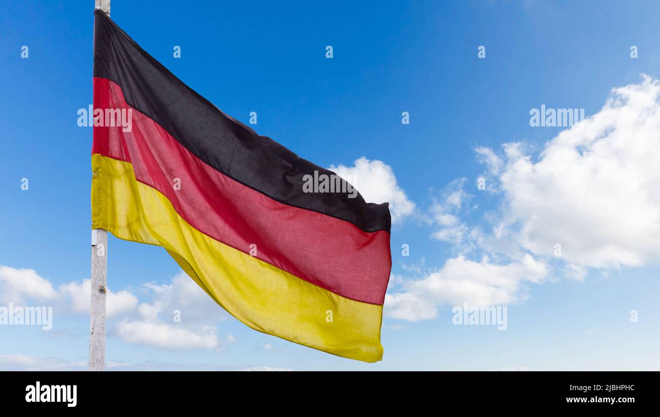 The official flag of Germany waving on a blue sky background ...