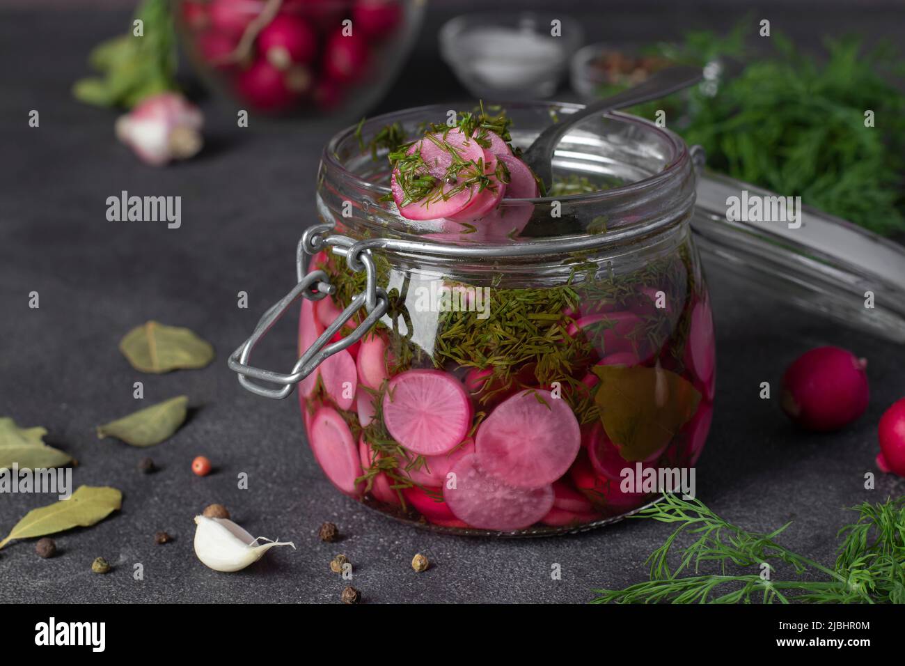 Marinated sliced radish with dill and garlic in open glass jar on brown ...