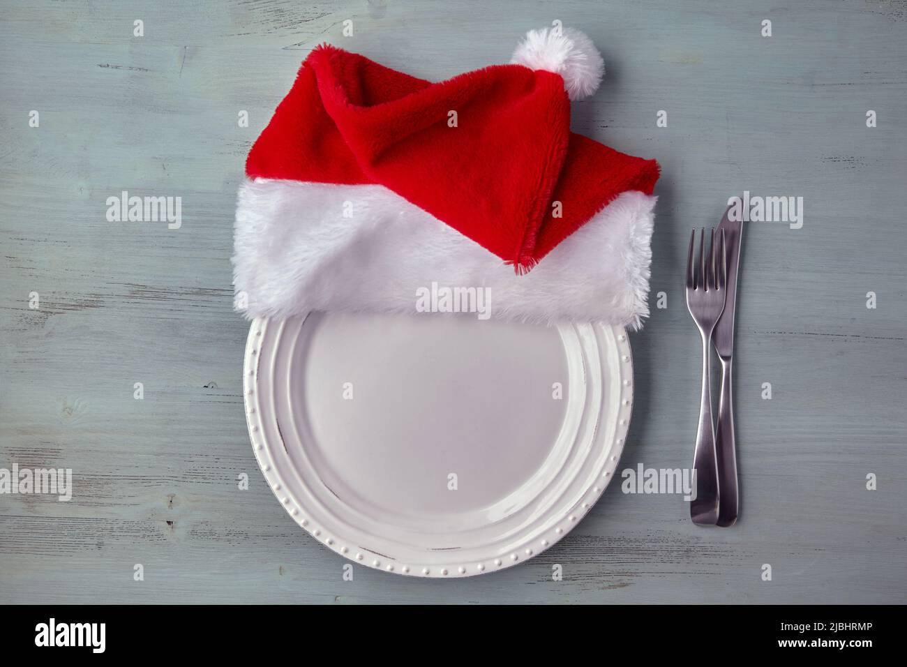 Empty white plate with a Christmas cap and cutlery on a blue wooden ...