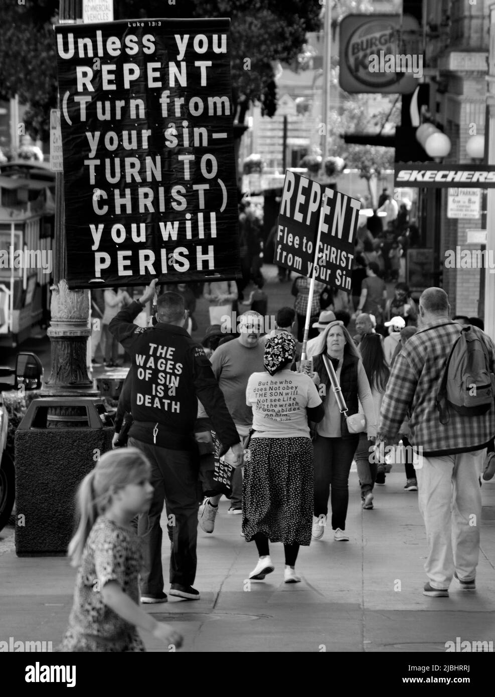 A religious couple carrying signs preach and evangelize on a sidewalk ...