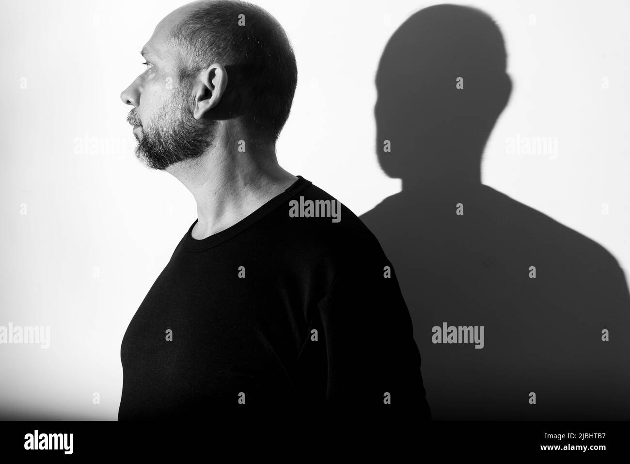 Portrait of a man and his shadow against white wall background ...