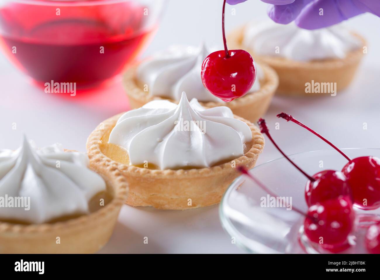 A woman pastry chef decorates a cake with a cocktail cherry. Production ...
