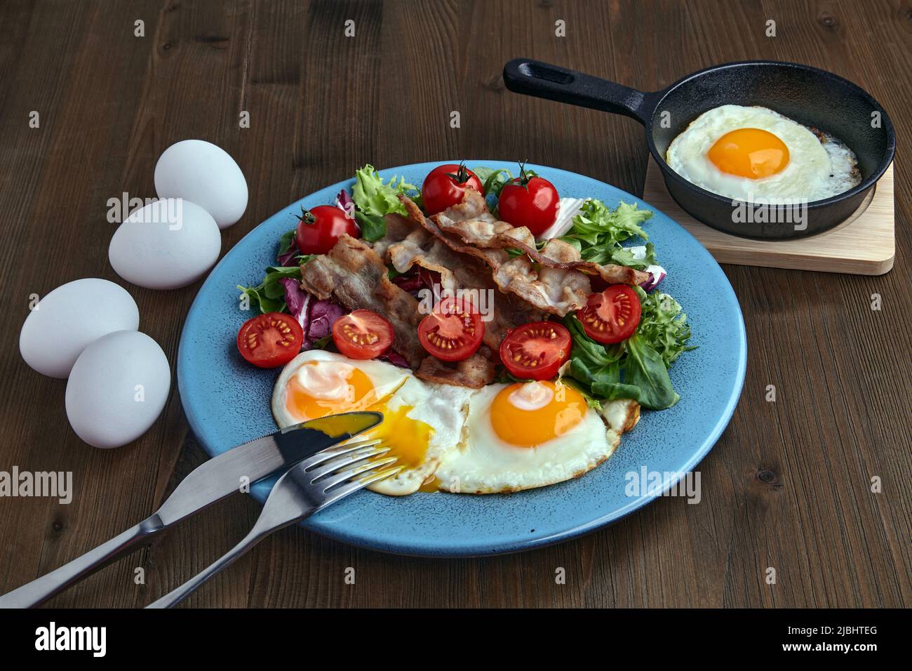 Fried eggs with bacon, lettuce and cherry tomatoes on a blue plate on a ...