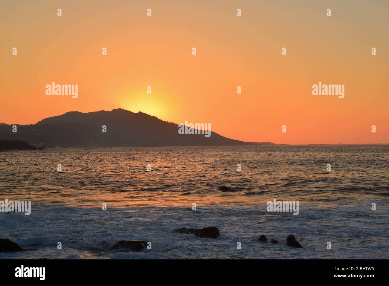 Sunset behind the hill by the ocean Stock Photo - Alamy