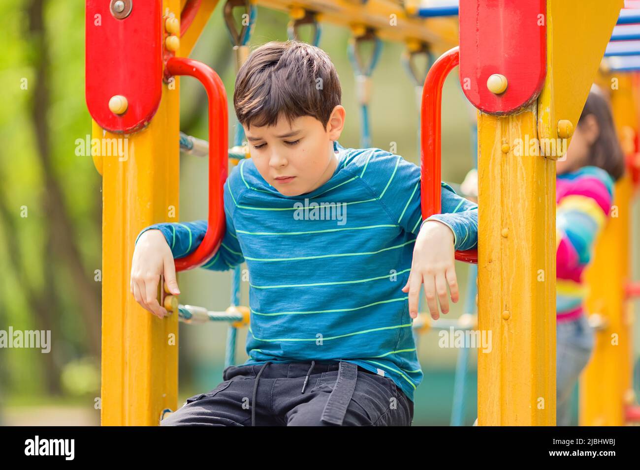 Sad and bored teen boy sitting on colorful playground in summer Stock ...