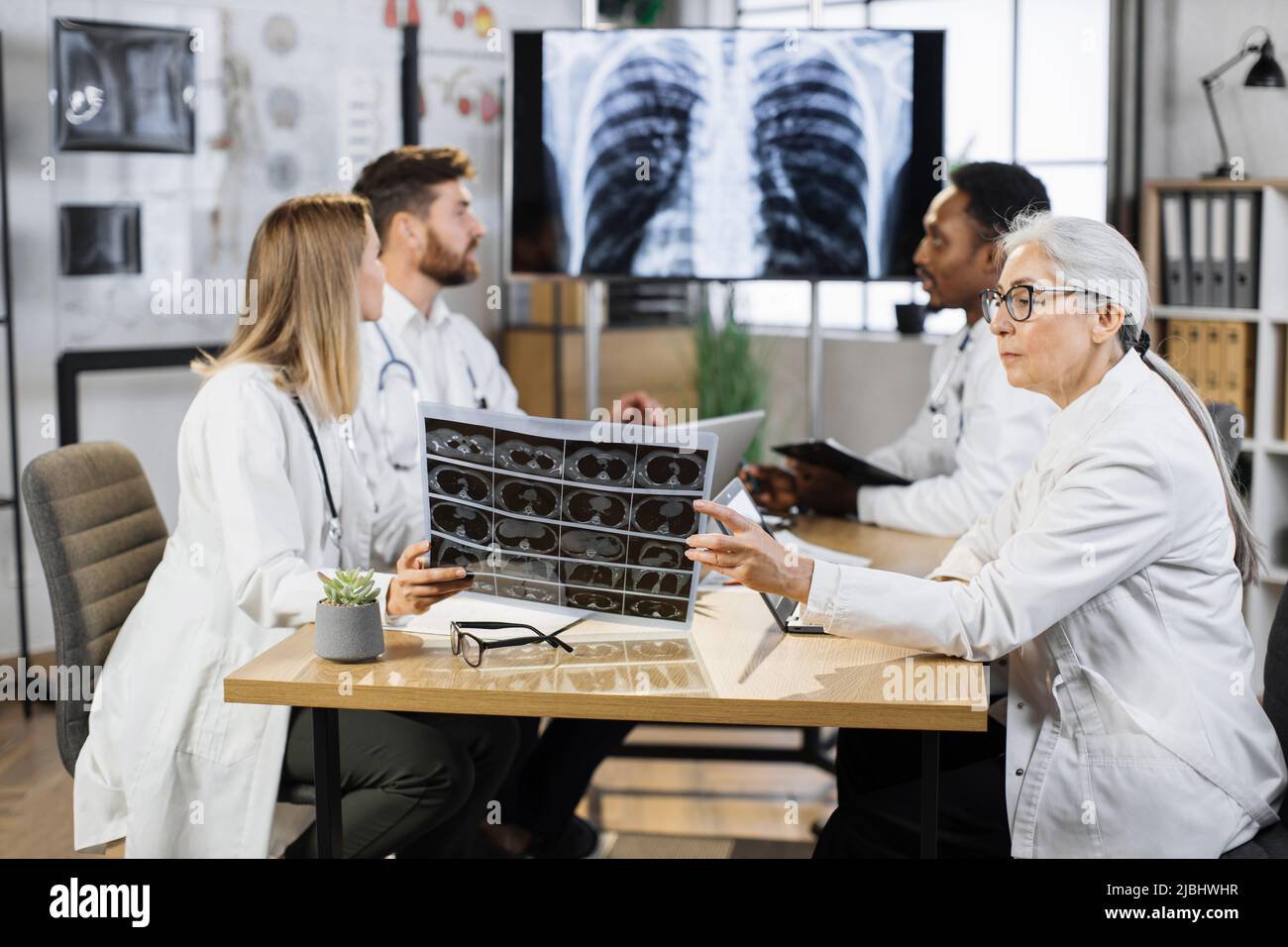 Multiracial doctors in lab coats discussing CT of patient while sitting ...