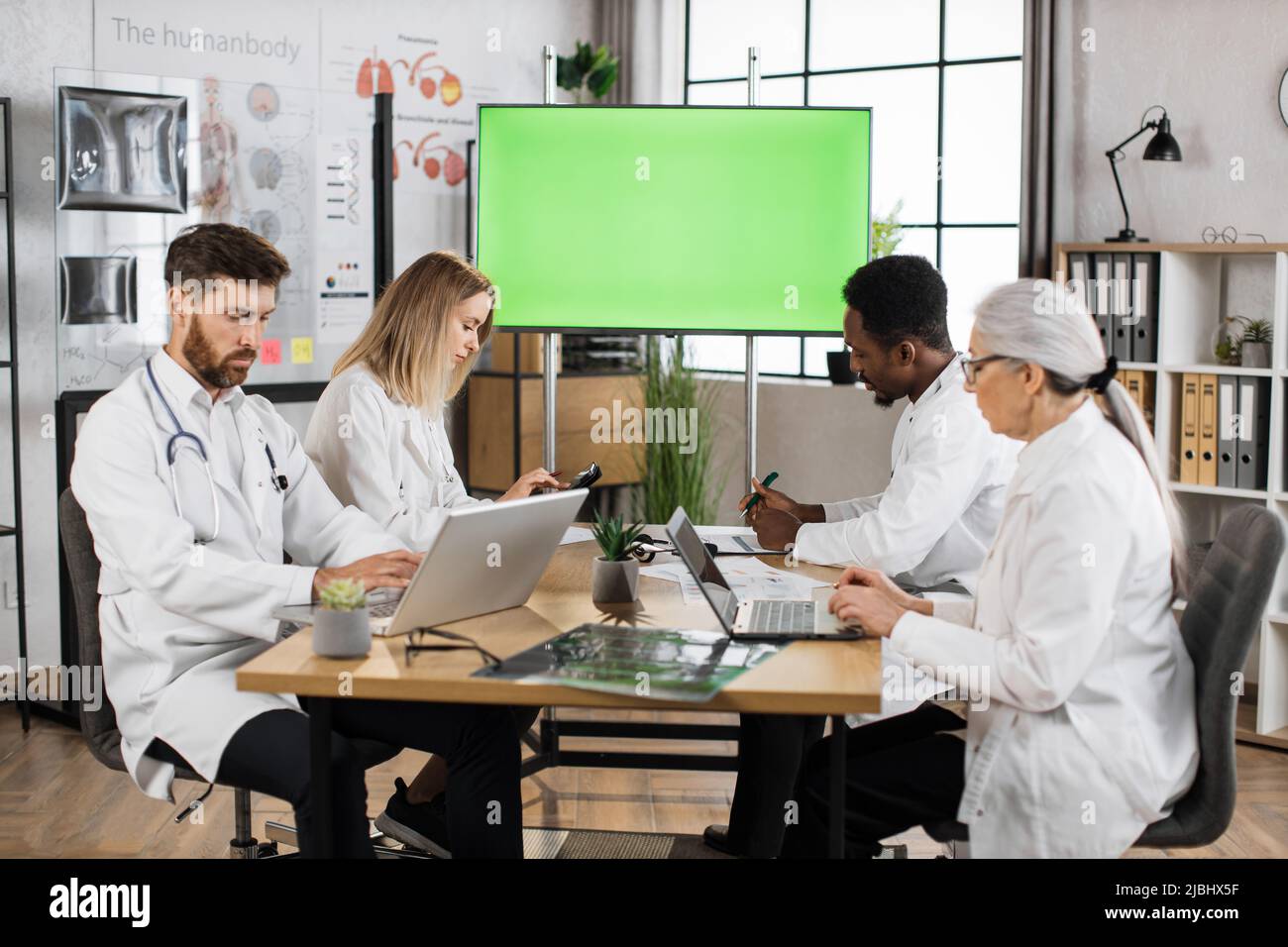 Focused male and female doctors sitting at desk and working on various ...