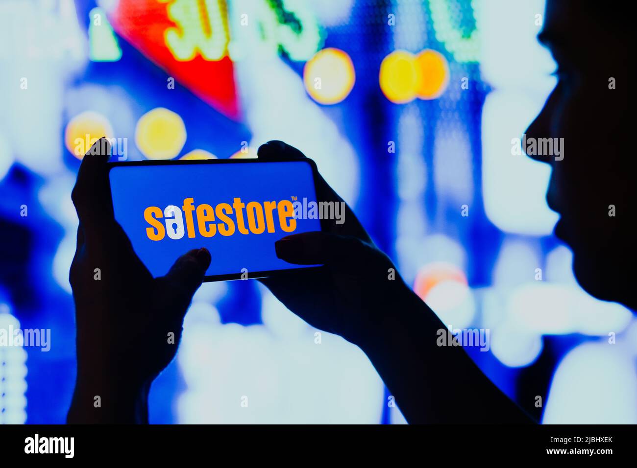 In this photo illustration, a silhouetted woman holds a smartphone with the Safestore logo ...