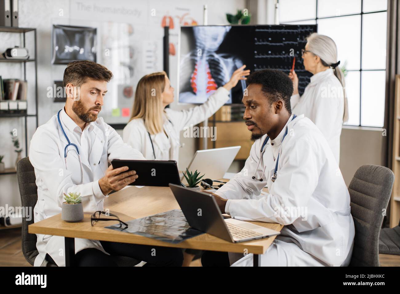 Competent male medical workers with laptop and tablet chatting together ...