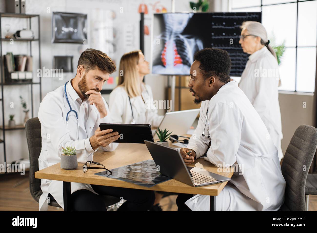 Competent male medical workers with laptop and tablet chatting together ...