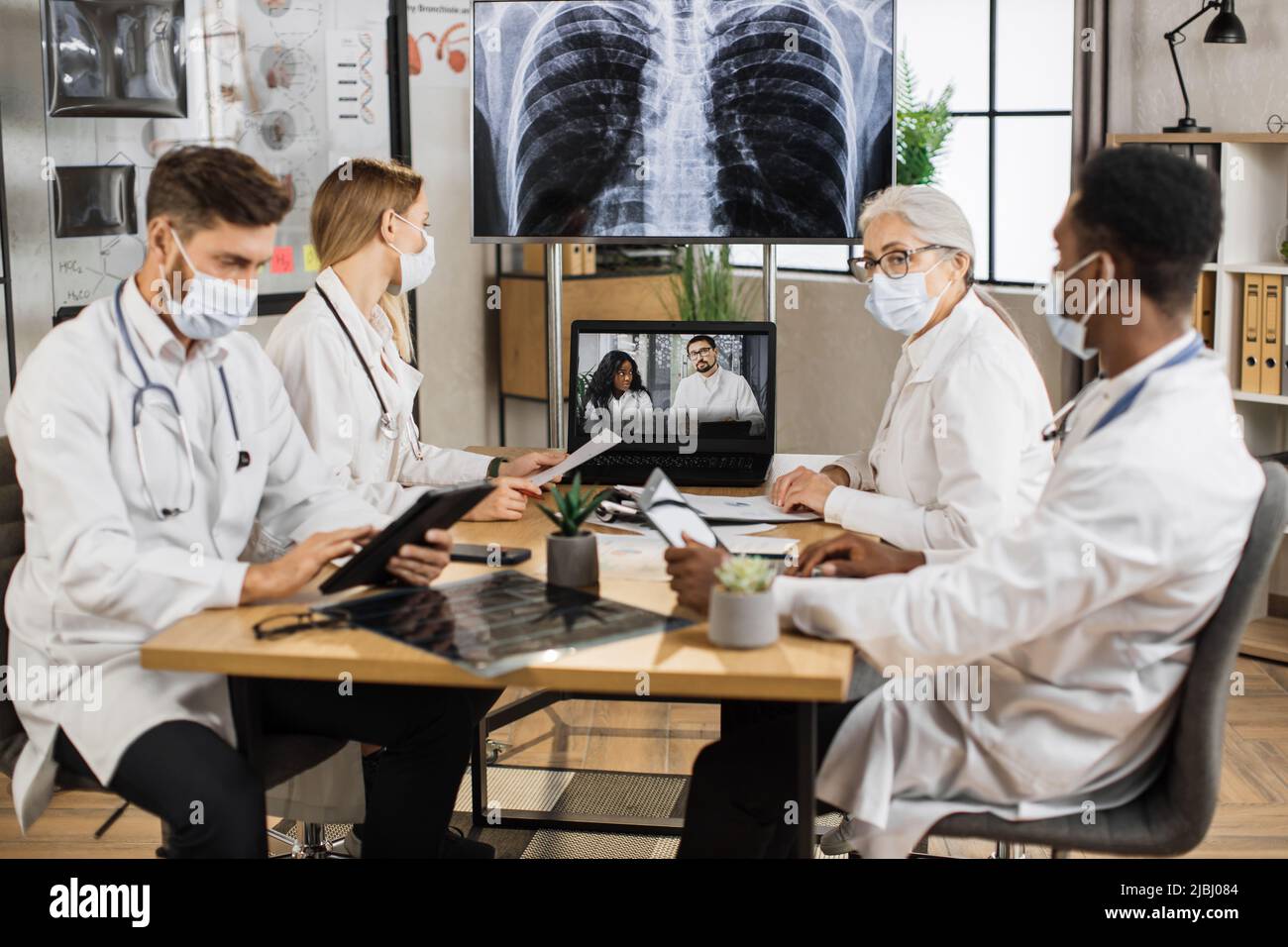 Group of multicultural doctors in sterile masks making notes on digital ...