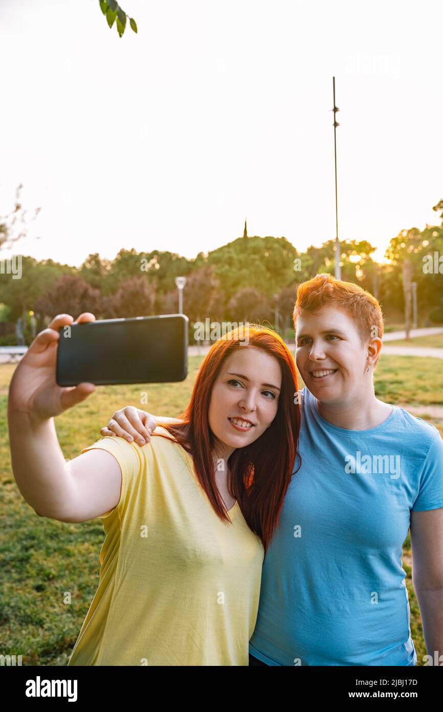 two great friends taking a selfie, in a public park in the city at sunset. young girls enjoying ...