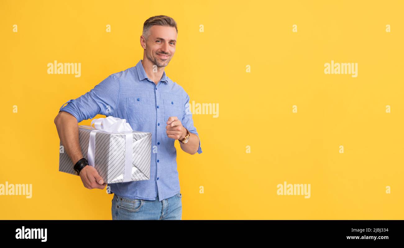 happy mature man hold box pointing finger on yellow background, copy ...