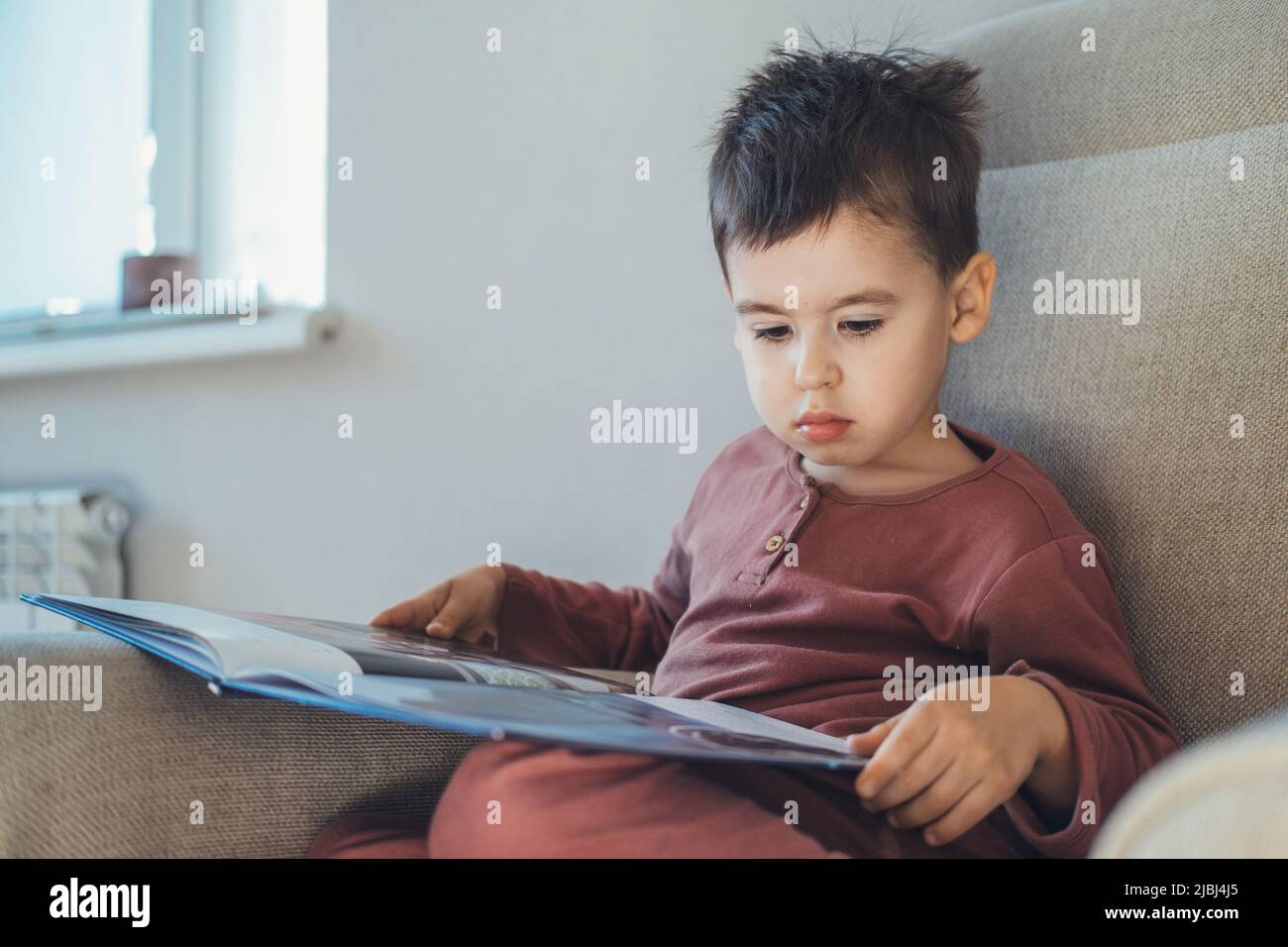 Portrait of little boy sitting on sofa and learn to read book alone ...