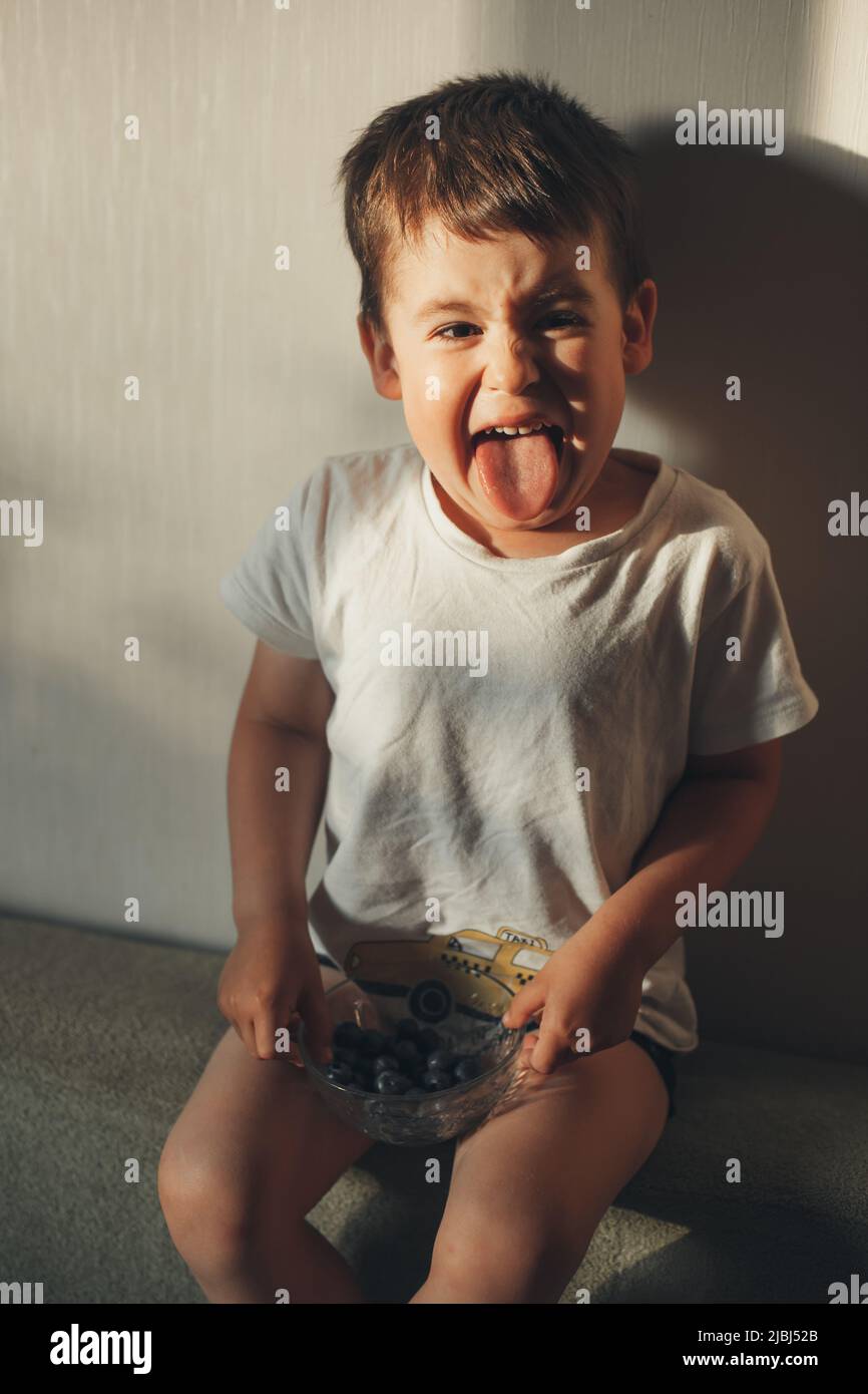 Boy sticking his tongue out eating blueberries from bow, having a ...