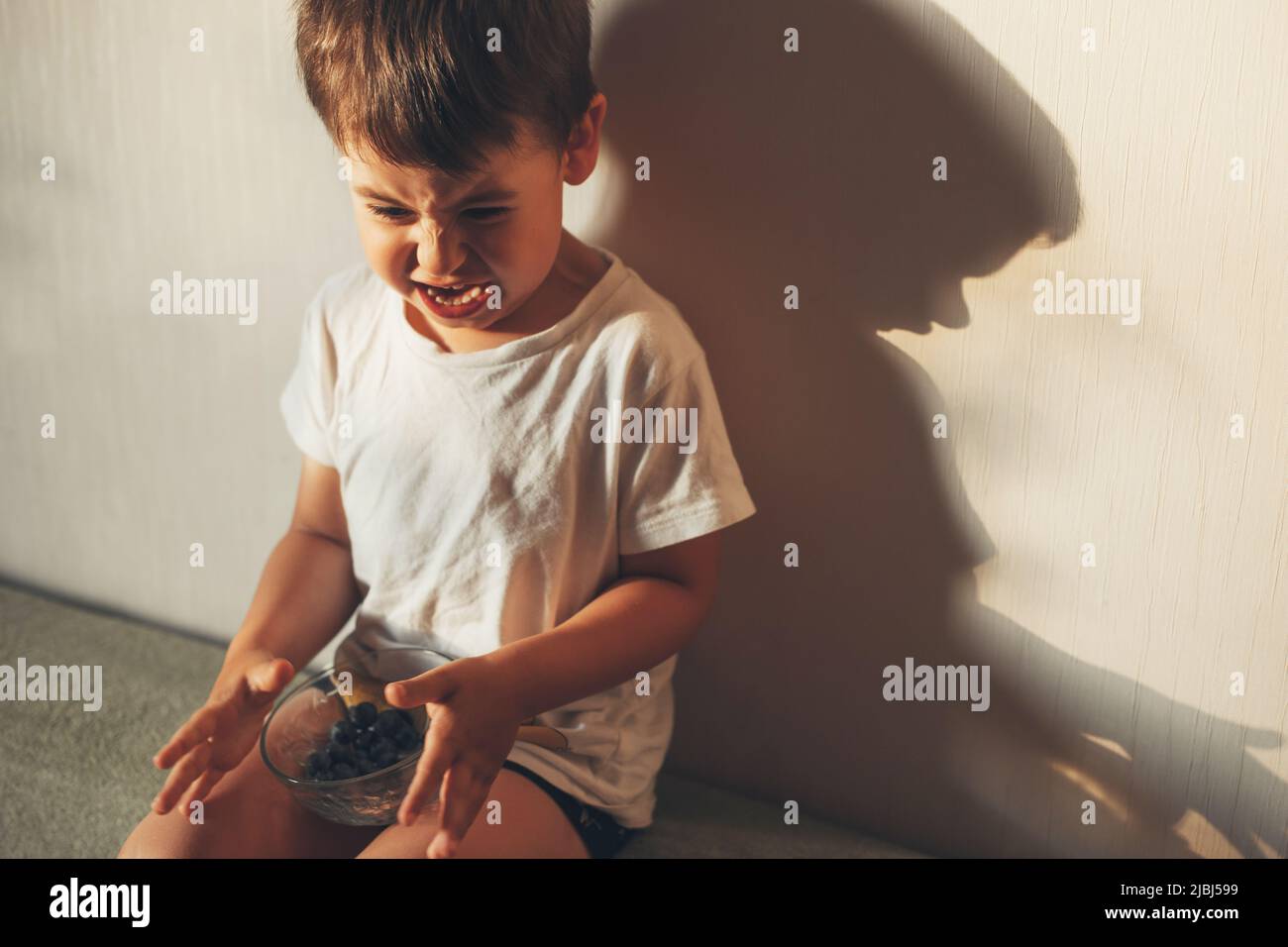 Caucasian boy tasting the sour blueberries, self-feeding the berry from ...