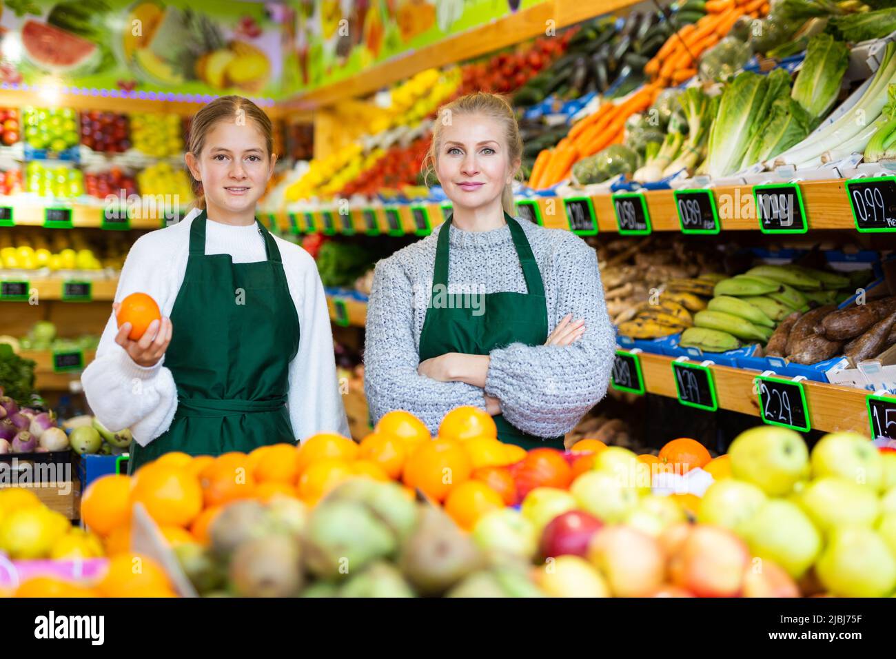Confident female owner of greengrocery store posing with teen daughter ...