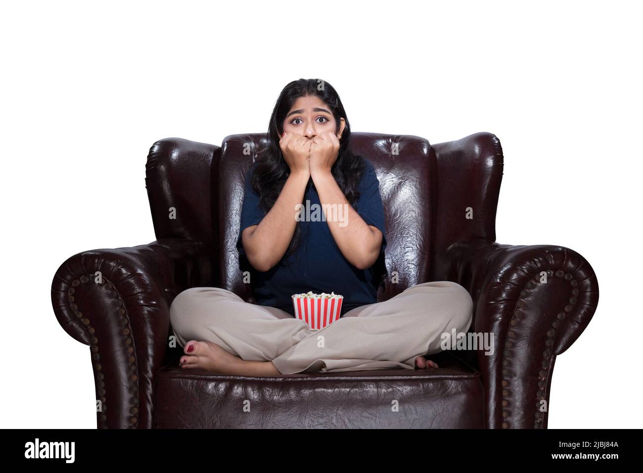 Asian woman with popcorn sitting on the couch with a scared expression ...