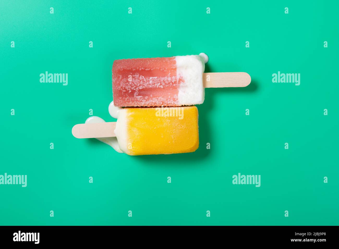 top view two vibrant color popsicles start melting on green background ...