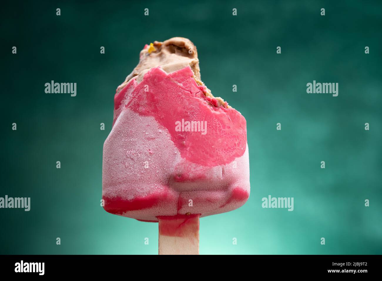 pink color chocolate outer popsicle with half eaten on a gradient green ...