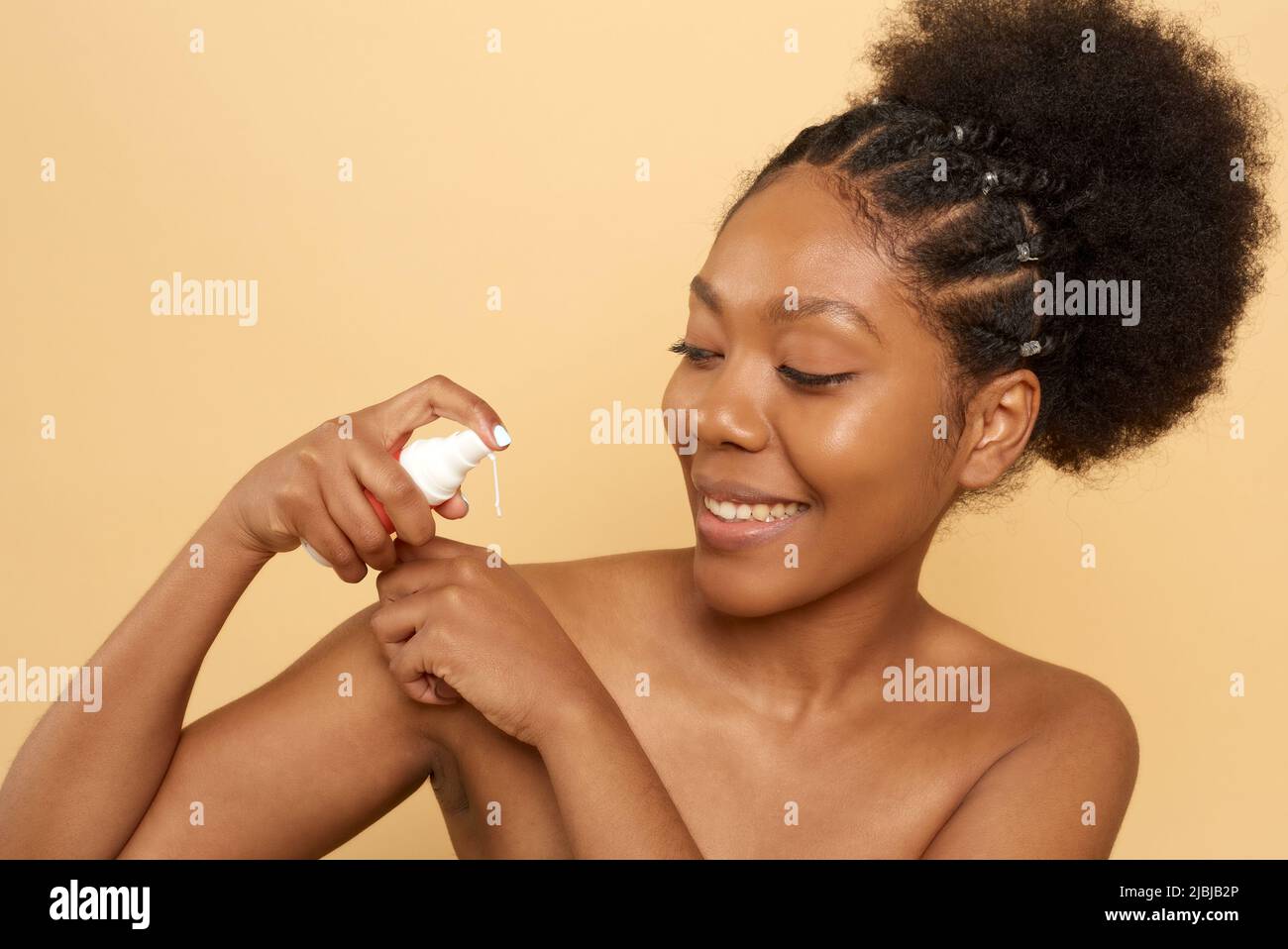 Dark-skinned woman with a wide smile, holds a moisturizer near her face ...