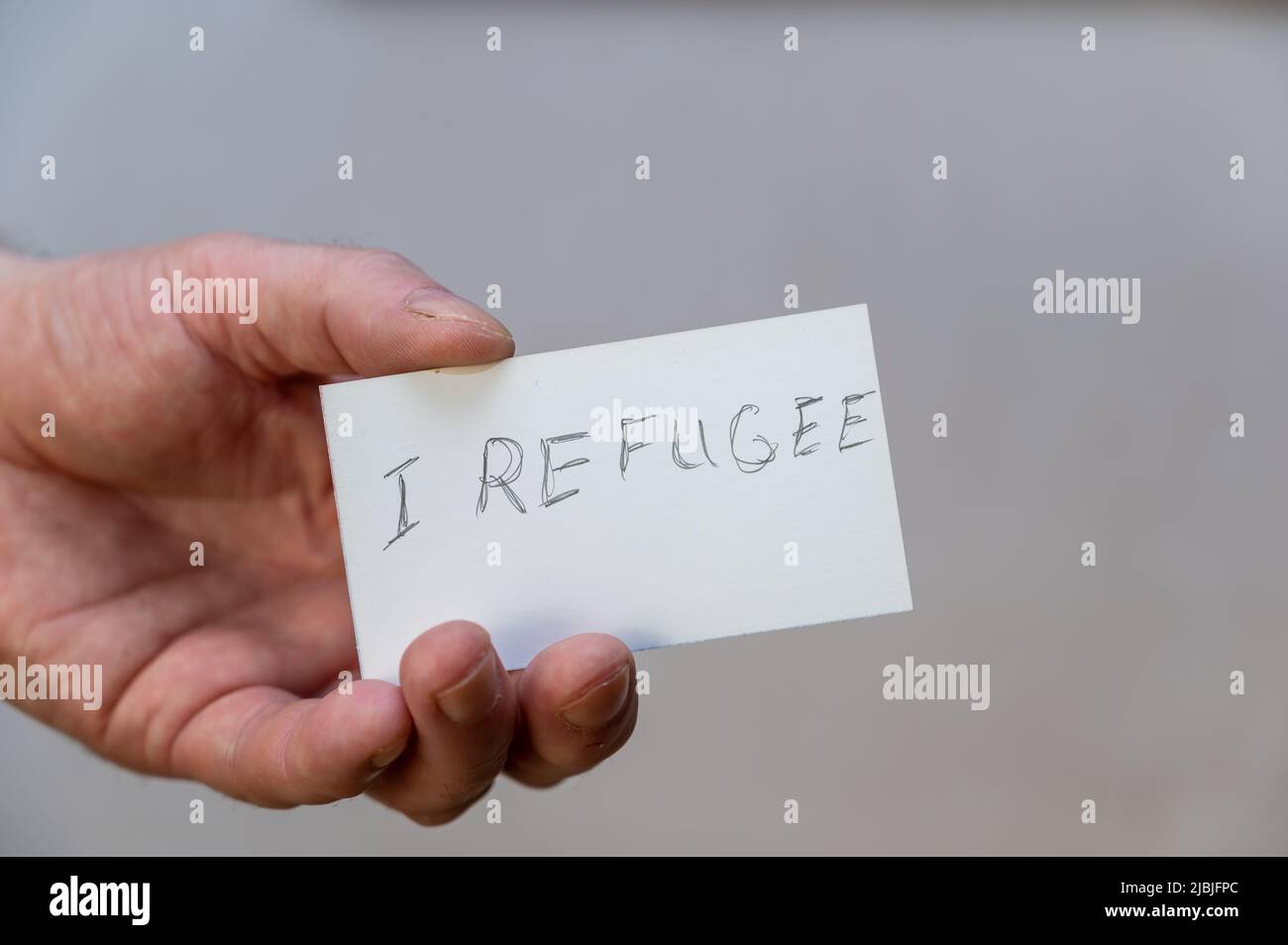 I refugee. Words written in jagged letters. A man's hand holds a white ...
