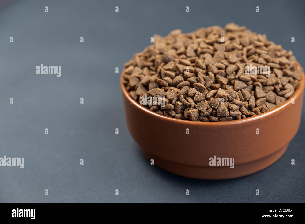 A full bowl of dry cat food against a gray background. Triangular ...