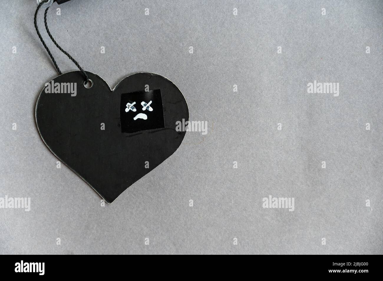 A black heart against a gray background. A sad face with crosses over ...