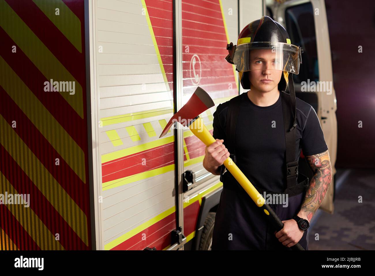 Photo of fireman wearing helmet with ax against fire engine Stock Photo ...