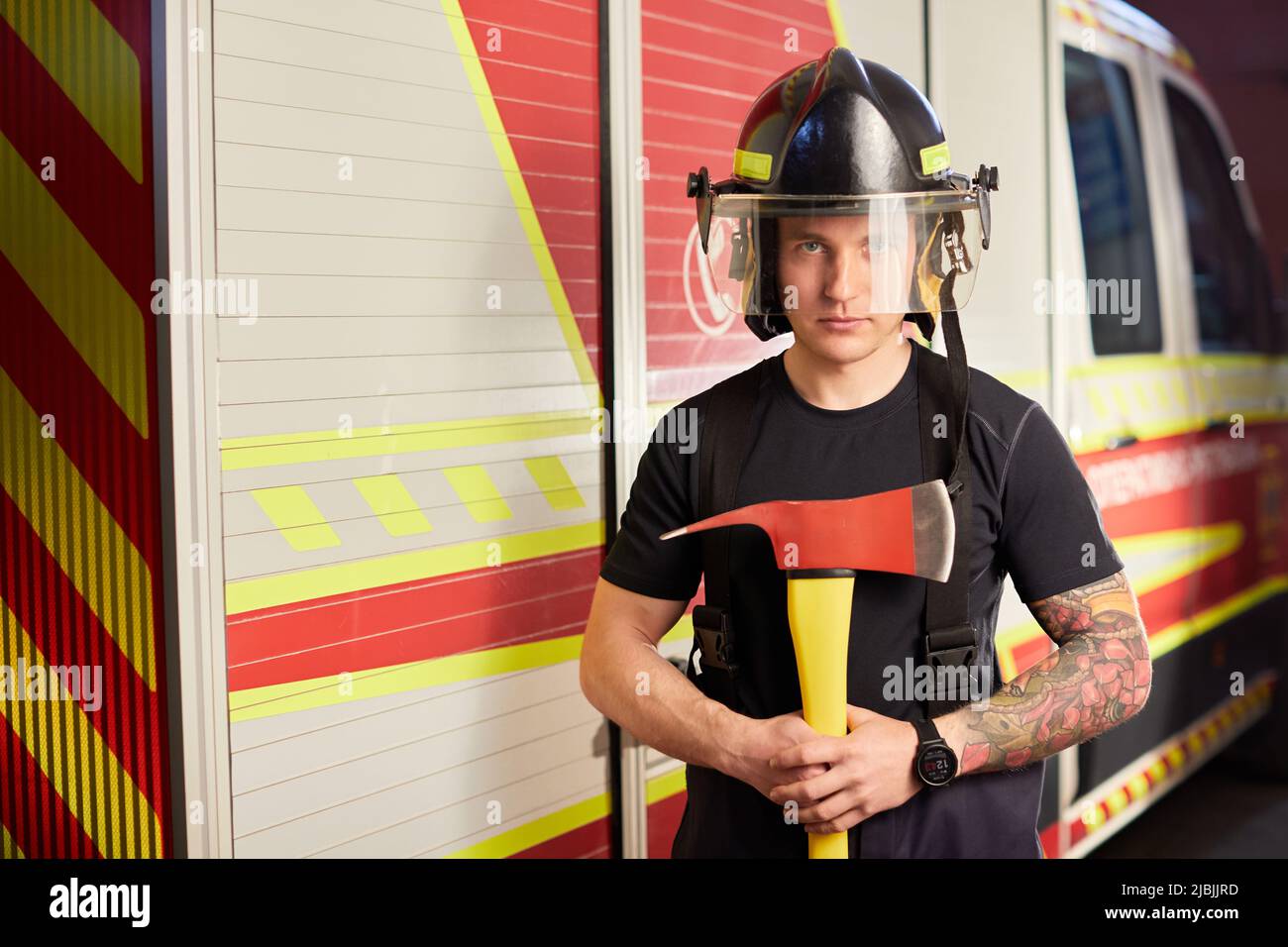 Photo of fireman wearing helmet with ax against fire engine Stock Photo ...