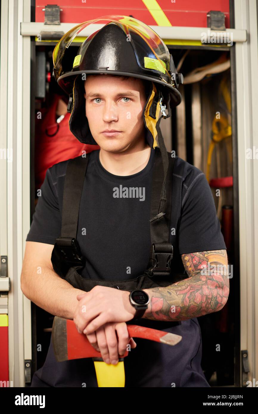 Photo of fireman wearing helmet with ax against fire engine Stock Photo ...