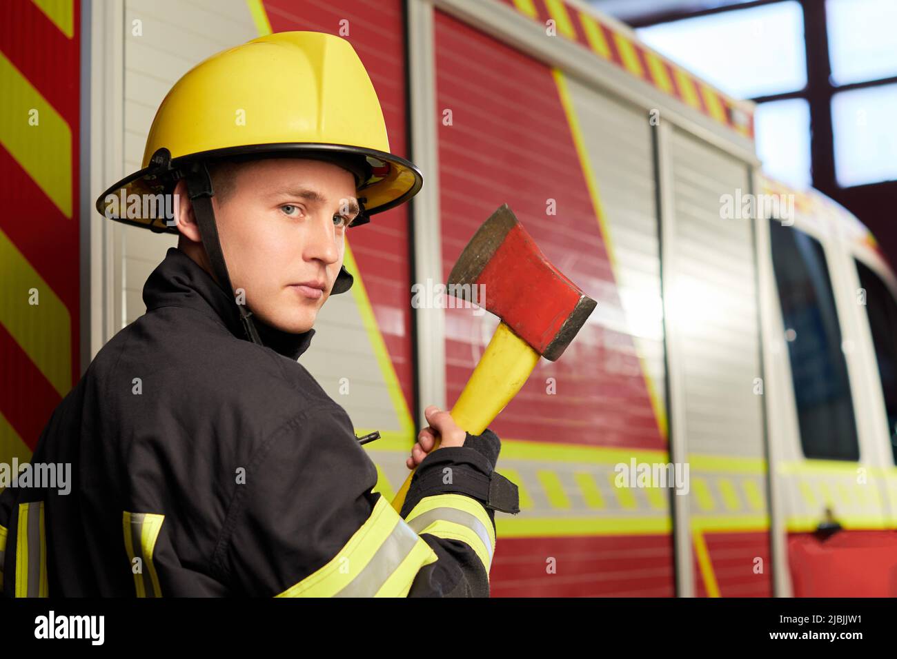 Firefighter fully equipped with helmet and ax in fire truck background ...