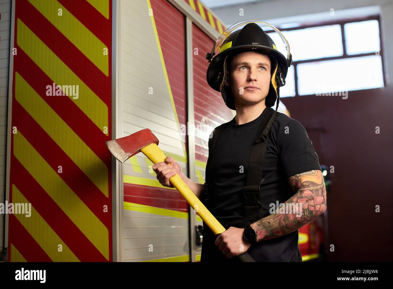 Photo of fireman wearing helmet with ax against fire engine Stock Photo ...
