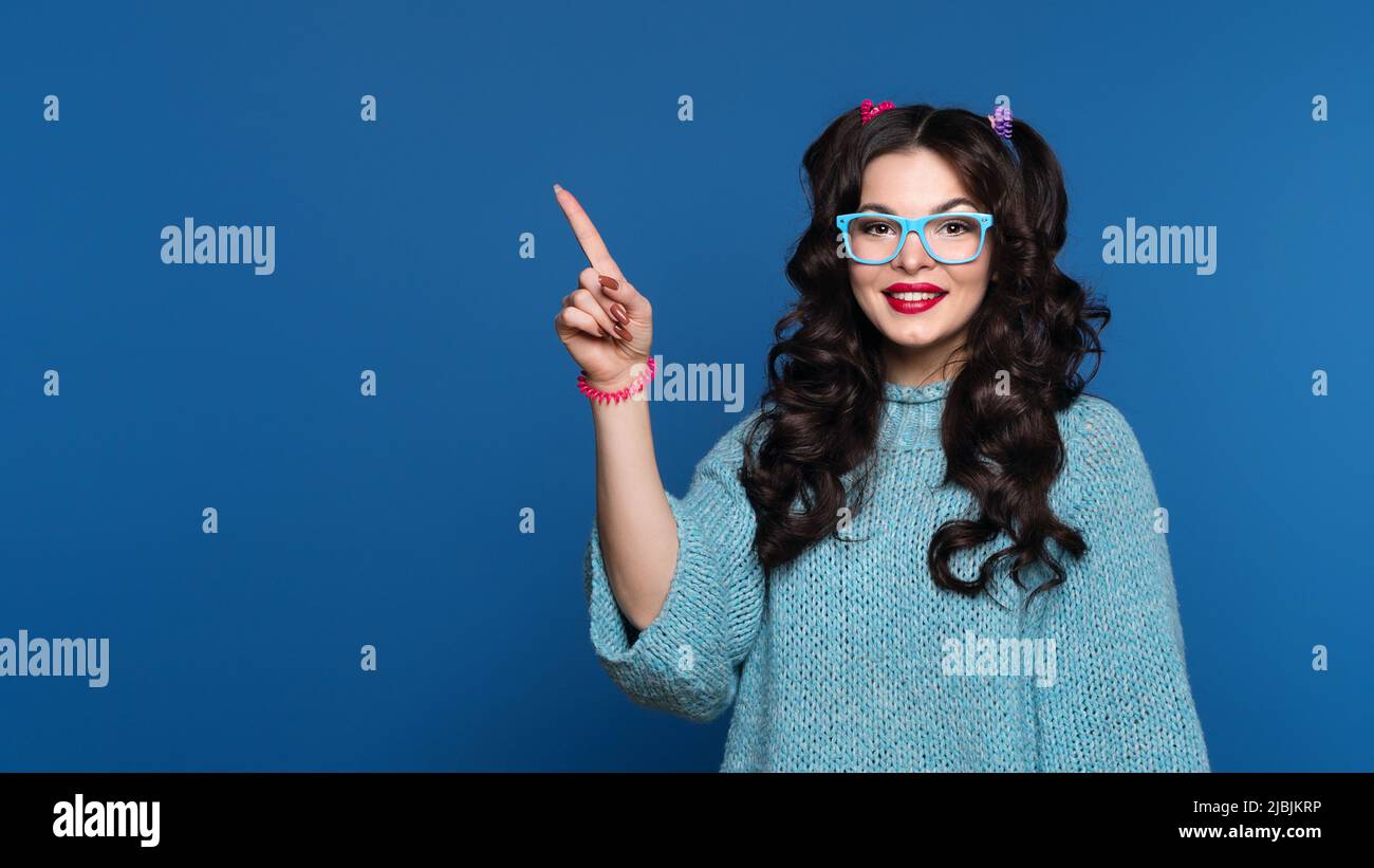 Carefree young girl with two ponytails pointing forefinger on blue ...