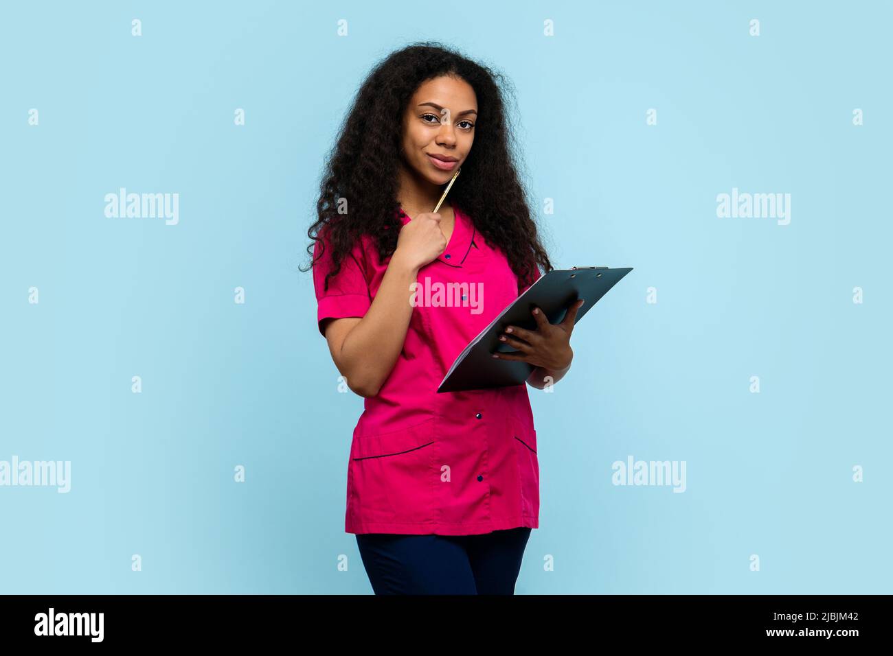Thoughtful Dark Skinned Female Nurse in Uniform filling medical form on ...